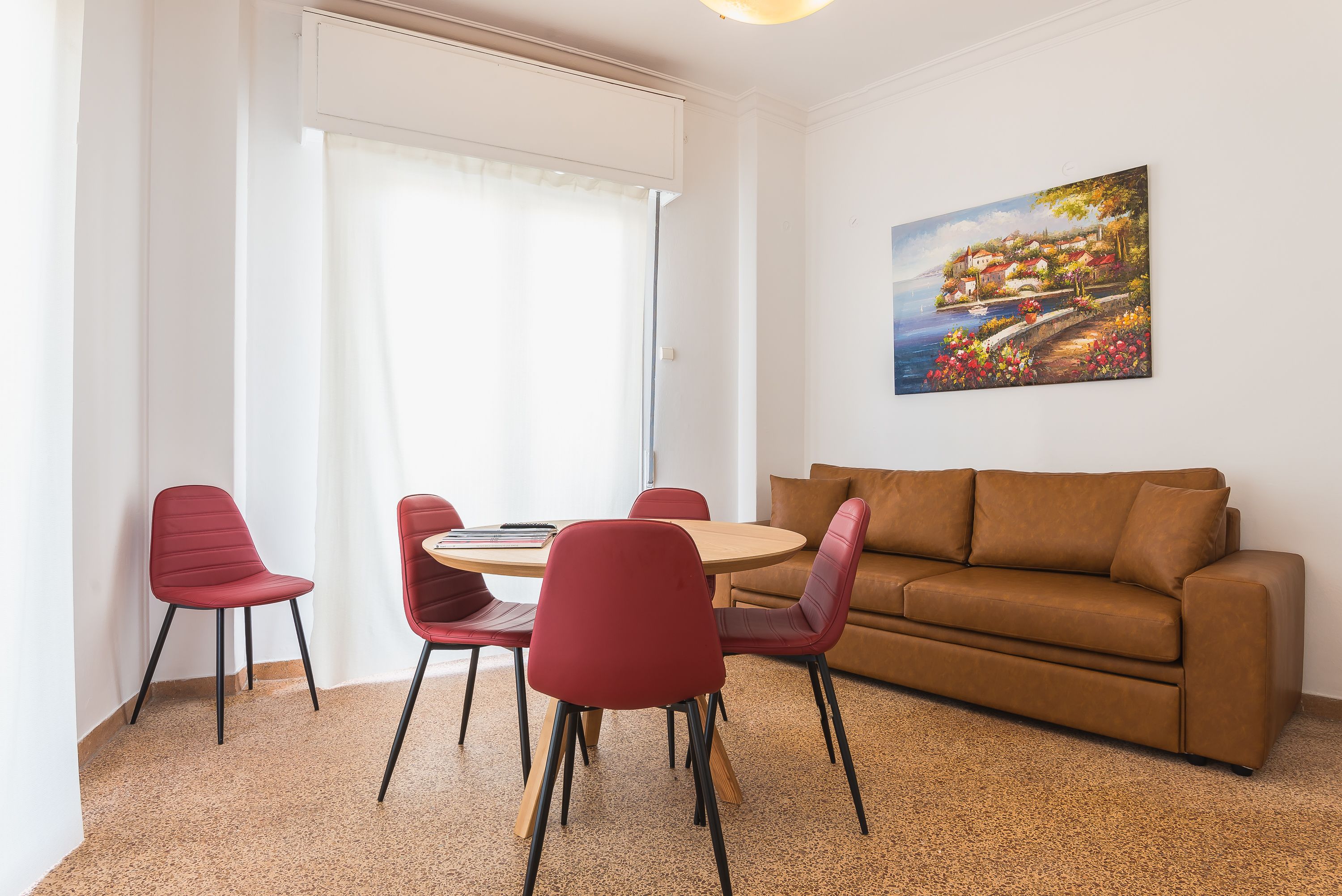 Uma sala de estar com um sofá marrom, cadeiras vermelhas e uma mesa redonda.