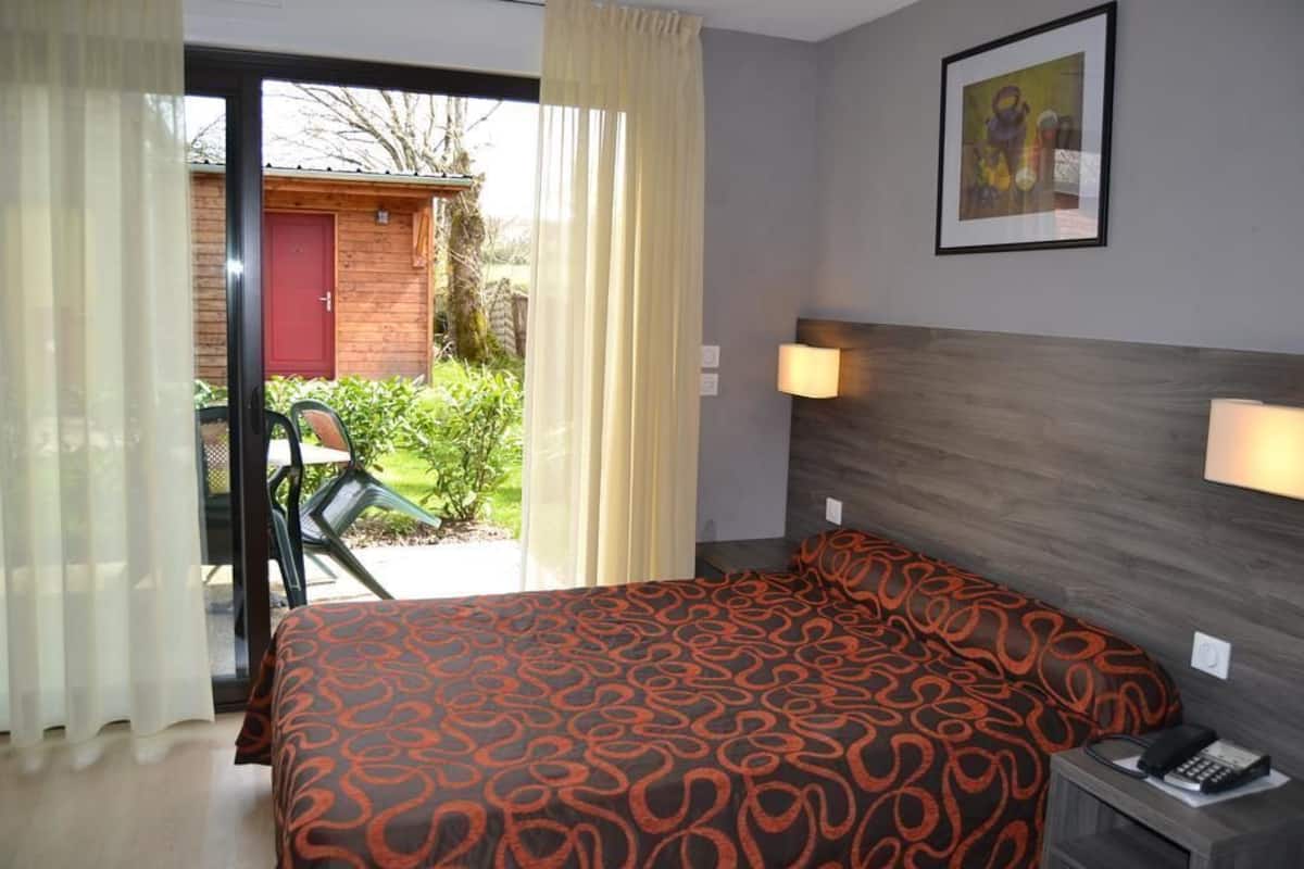 Quarto com cama, mesa de cabeceira, luminária, telefone e vista para um jardim.