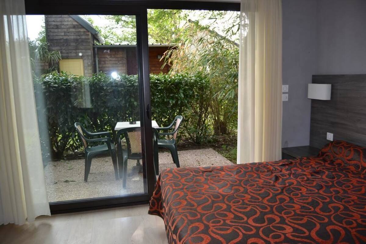 Quarto com cama, janela com cortinas e vista para área externa com mesa e cadeiras.