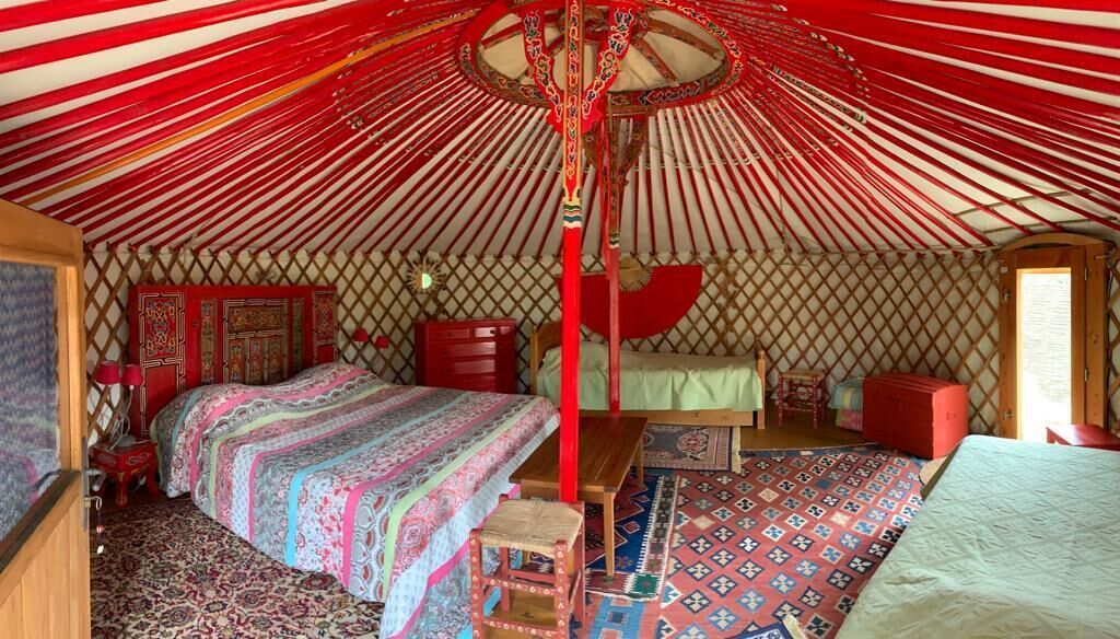 Uma yurta tradicional com telhado riscado em vermelho e branco, um mastro de madeira central e chão estampado.