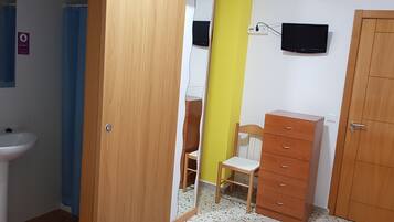 Quarto com guarda-roupa de madeira, uma cadeira, um pequeno armário, televisão na parede e uma pia.