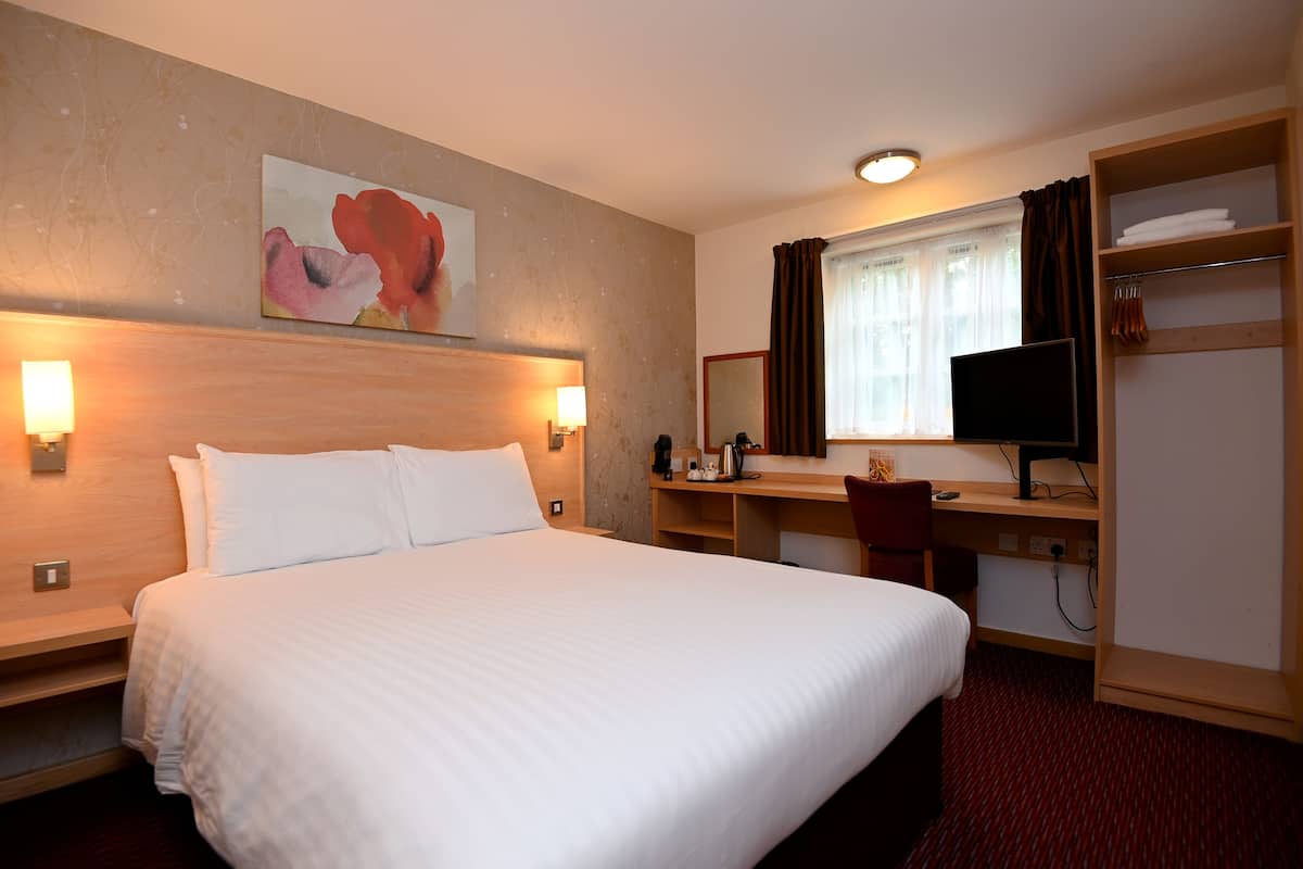 Quarto de hotel com uma cama grande, uma escrivaninha com computador, uma cadeira, televisão e guarda-roupa.