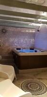 Uma área de spa com parede de pedra, banheira de hidromassagem e cadeiras brancas.
