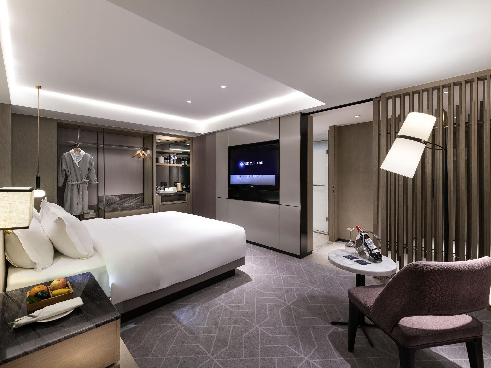 Quarto de hotel moderno com cama, televisão, área de estar e guarda-roupa.