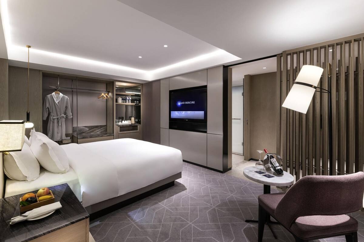 Quarto de hotel moderno com cama, televisão, área de estar e guarda-roupa.