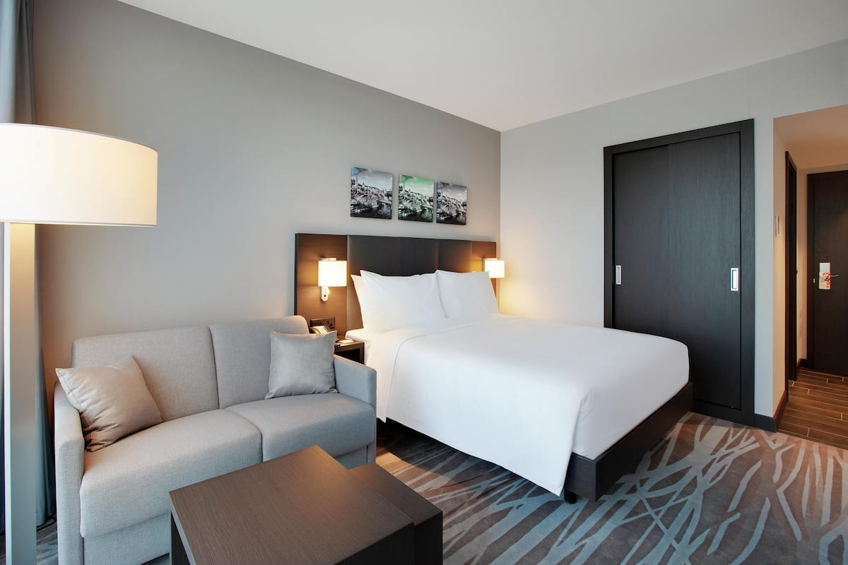 Quarto de hotel com uma cama, um sofá, uma mesa de cabeceira e uma luminária.