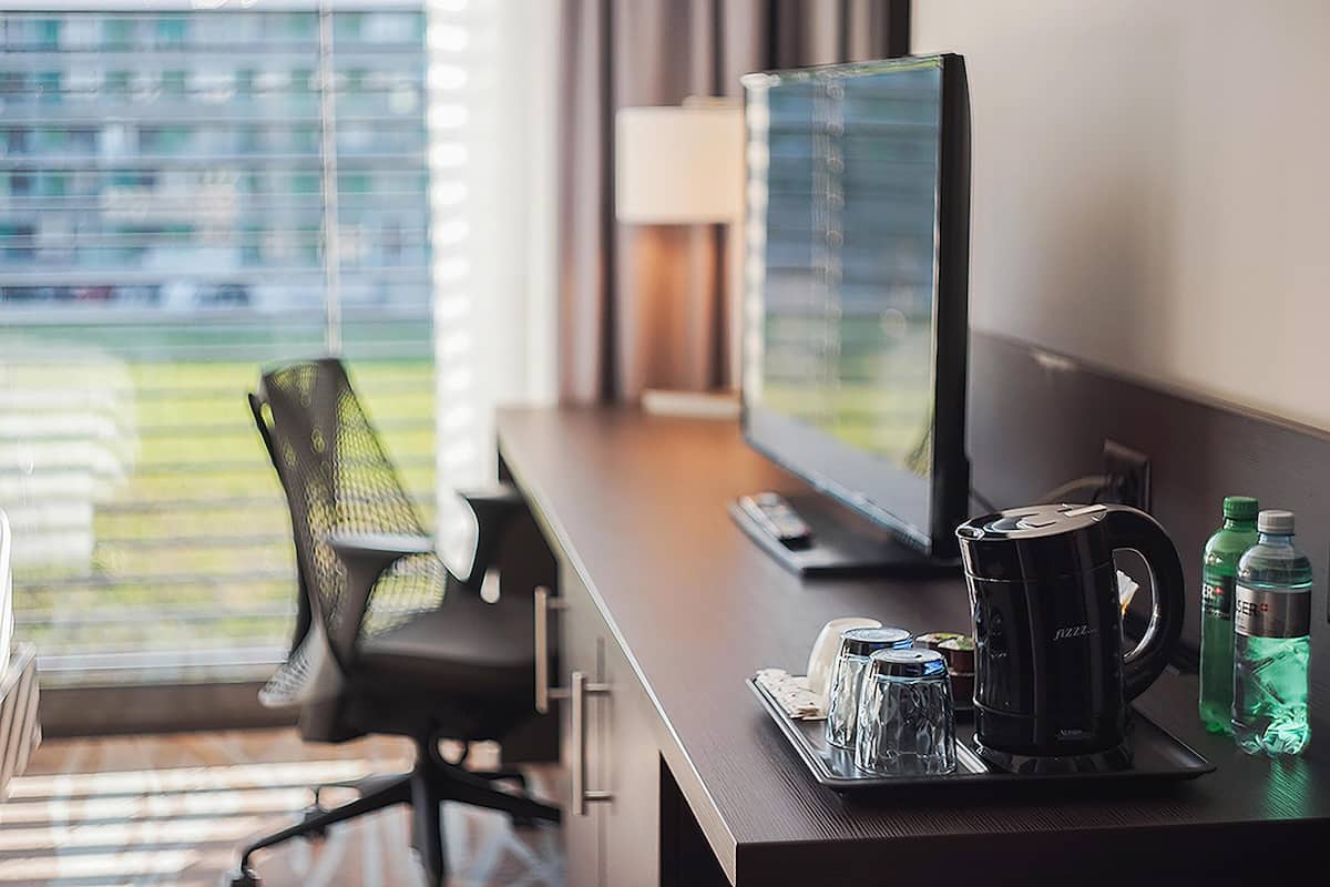 Quarto de hotel com escrivaninha, computador, máquina de café e duas garrafas de água.