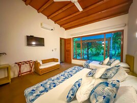 Quarto com uma cama grande, televisão, ventoinha no teto e vista para um jardim através de uma porta de correr.