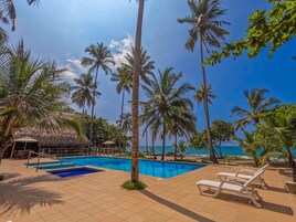 Uma área de piscina com espreguiçadeiras, palmeiras e vista para o oceano.