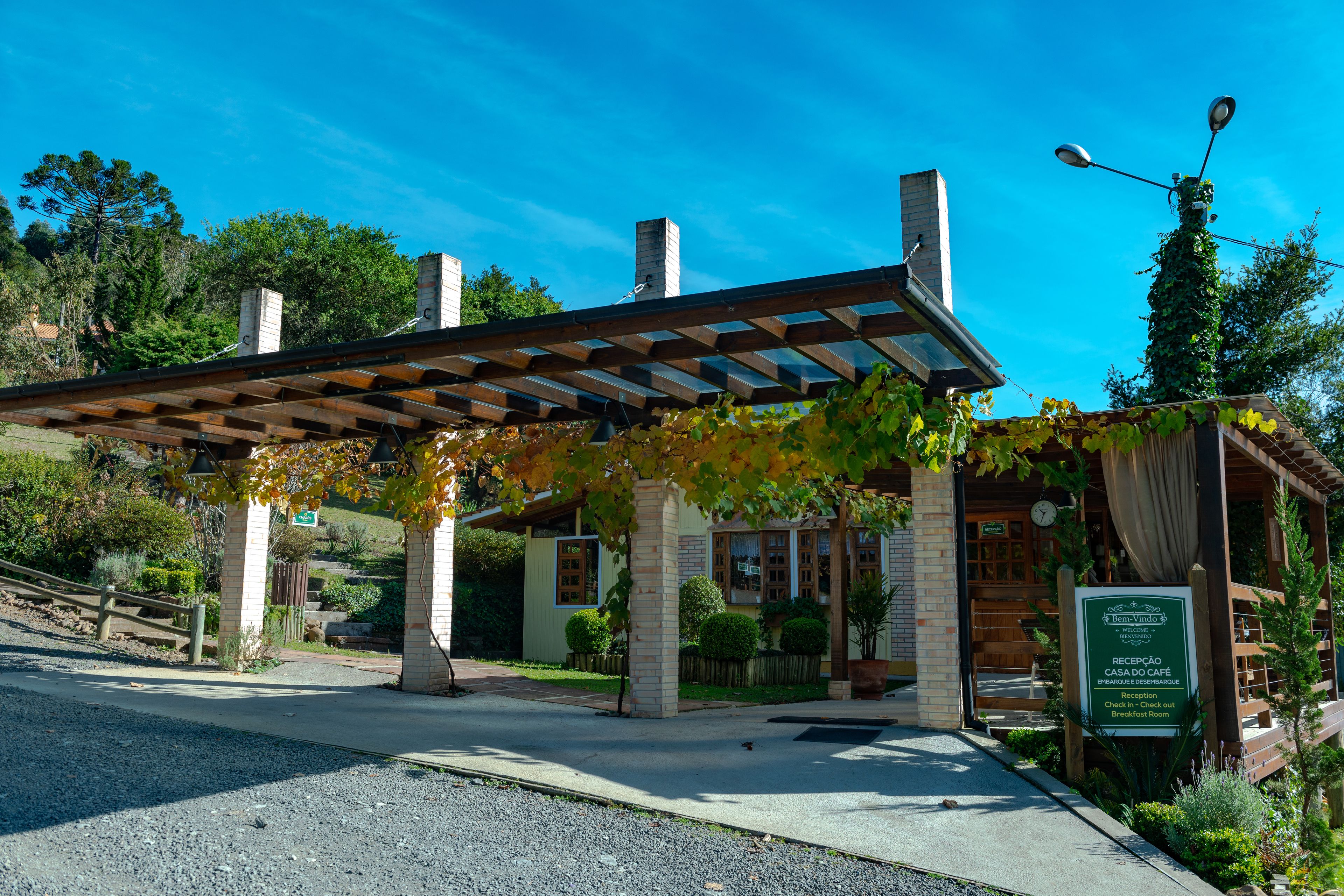 Um edifício com entrada coberta por uma pérgola, pilares de tijolo e uma placa indicando a área de recepção.