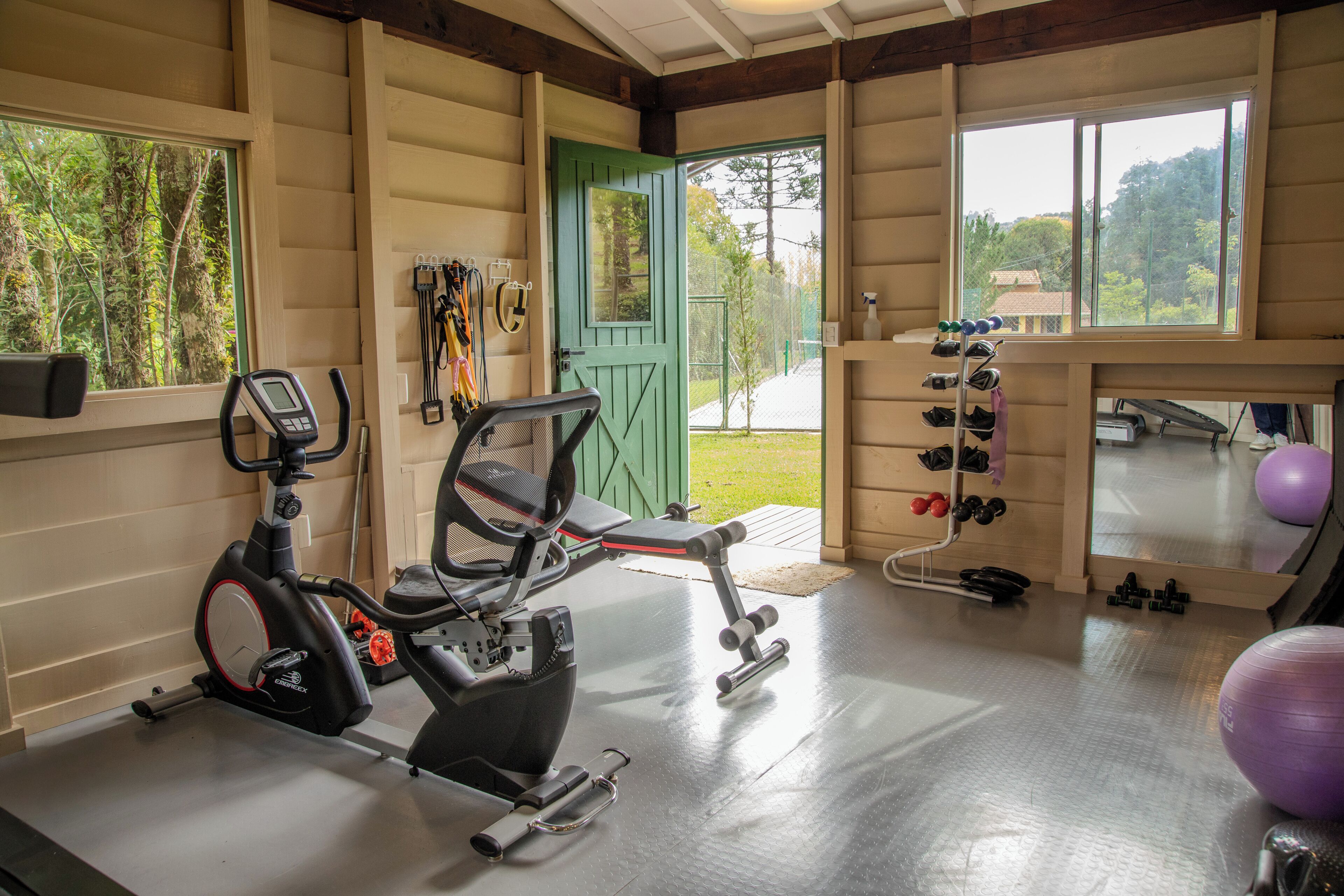 Uma academia em casa com uma bicicleta ergométrica, esteira e diversos pesos.