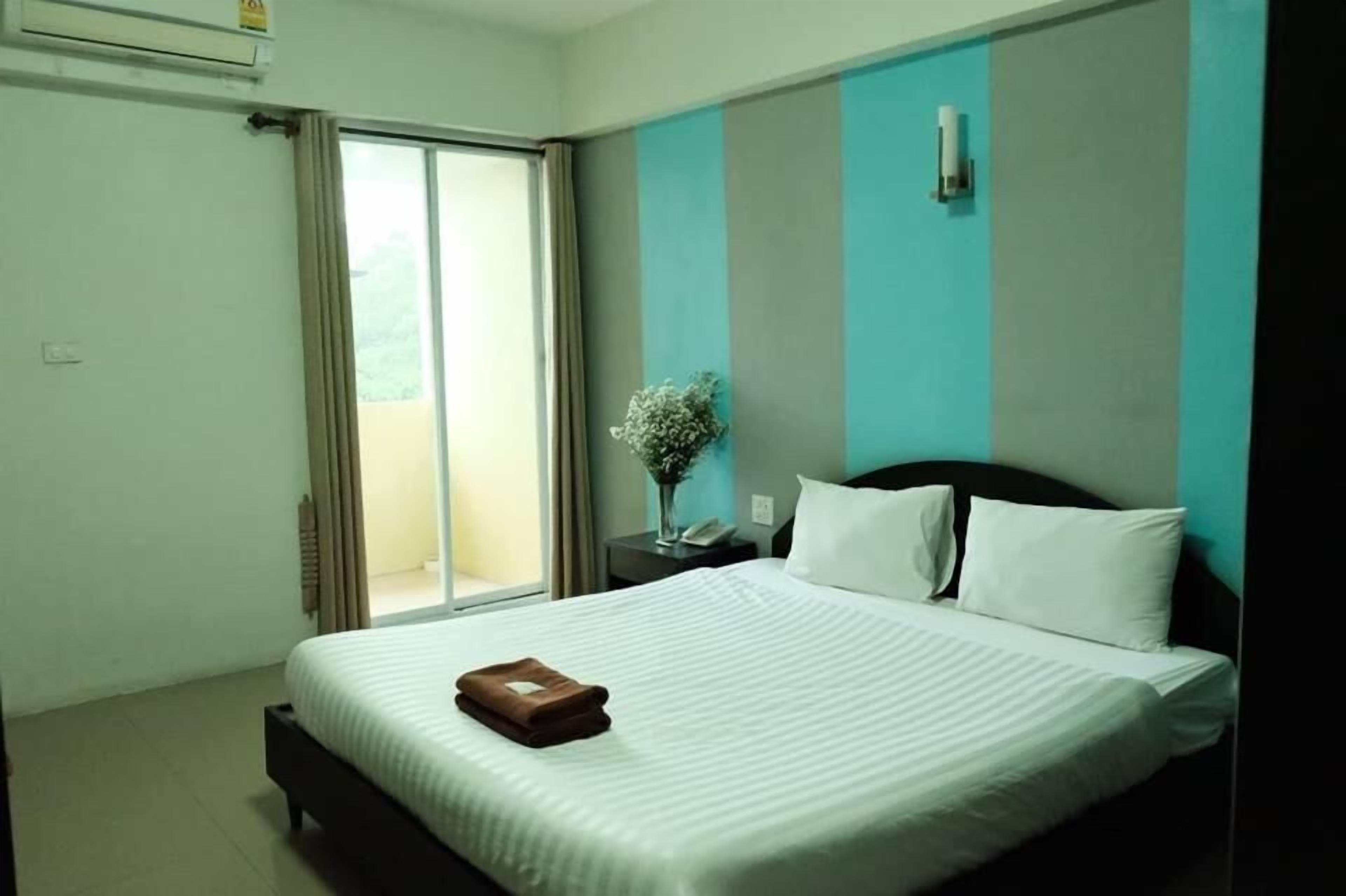 Quarto de hotel com cama, mesa de cabeceira, um vaso com flores e uma porta de correr para o exterior.