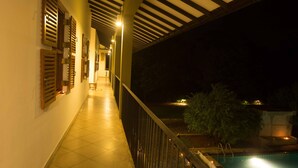 Uma varanda coberta com piscina, piso de azulejos e persianas de madeira na parede.