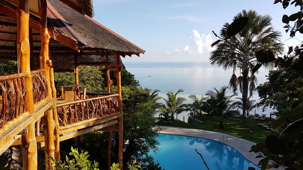 Uma estrutura de madeira com varanda com vista para uma piscina e o mar.