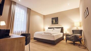 Quarto de hotel com cama, secretária, cadeira e abajur.