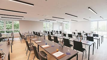 Uma sala de conferências com várias mesas e cadeiras, janelas amplas e iluminação embutida no teto.
