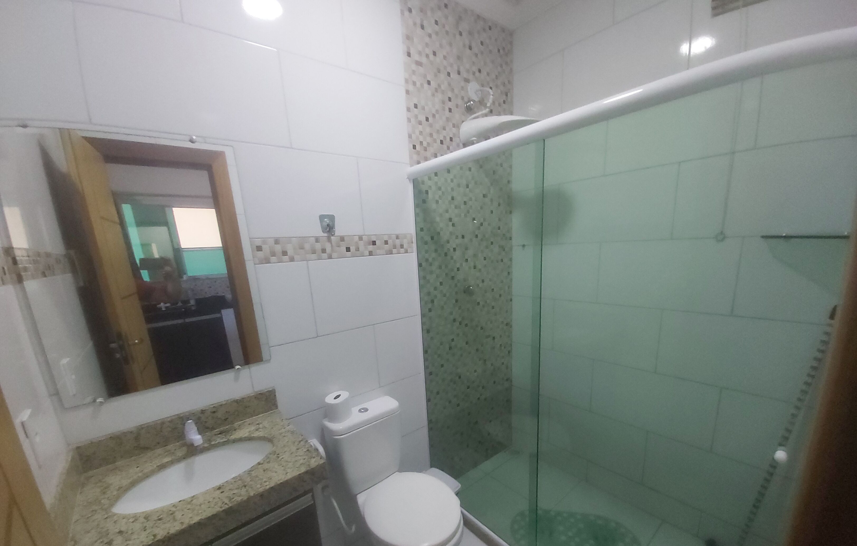 Casa de banho com lavatório, sanita e cabine de duche em vidro.