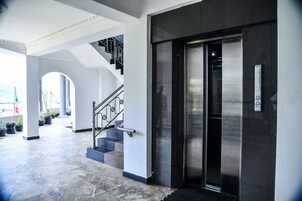 Entrada de um edifício moderno com escadas, elevador e plantas em vasos.