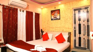 Quarto de hotel com cama, cortinas vermelhas, um quadro na parede e um aparelho de ar condicionado.