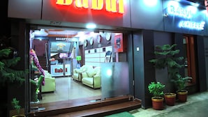 Entrada de um hotel com balcão de recepção, uma placa com o nome 'Babu' e plantas em vasos na parte externa.