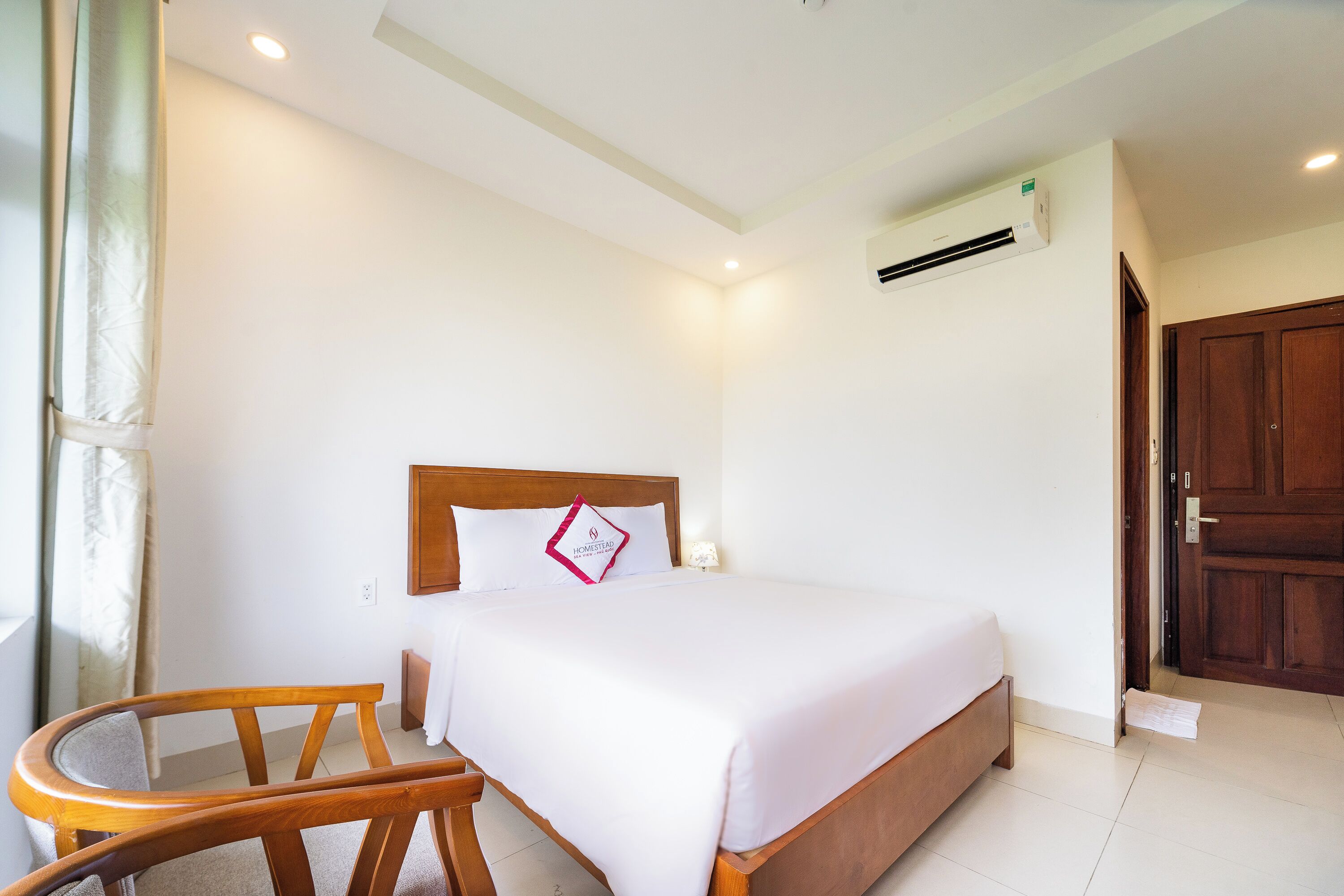 Quarto de hotel bem arrumado com uma cama grande, uma cadeira de madeira, uma mesa de cabeceira e uma porta.