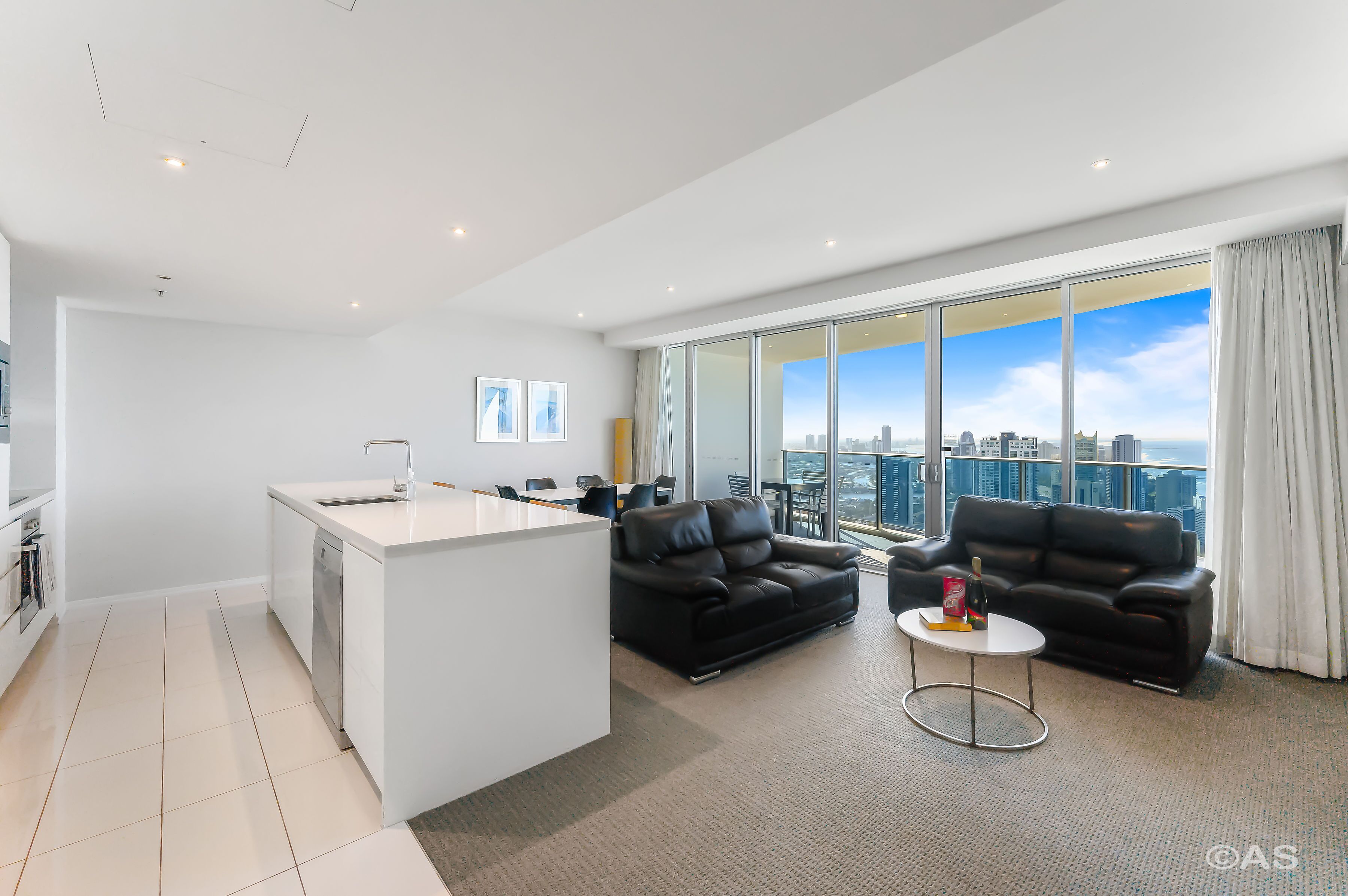 Uma sala de estar moderna com um sofá de couro preto, uma mesinha redonda e uma janela grande com vista para a cidade.