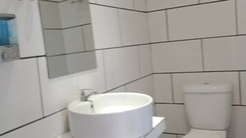 Um banheiro com azulejos brancos, um lavatório redondo, vaso sanitário e um espelho.