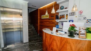 Uma área de recepção de hotel com um balcão de madeira, um mostrador de atendimento, um globo e uma placa indicando política de proibido fumar.