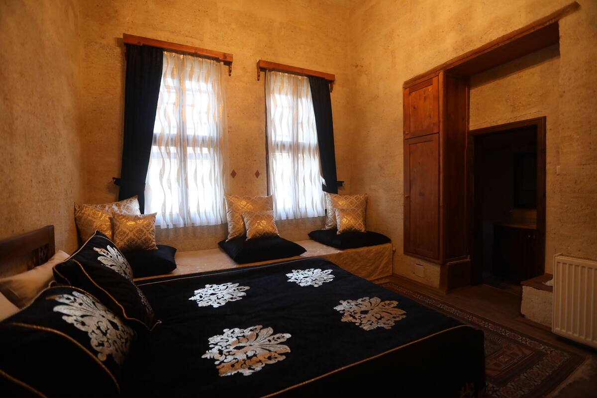Quarto com uma cama grande, duas janelas com cortinas, um guarda-roupa de madeira e um radiador.