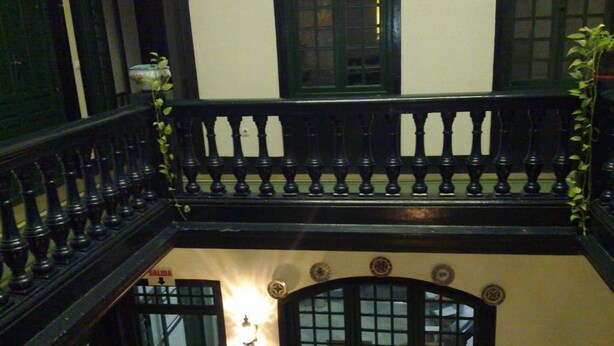 Uma varanda com guarda-corpo preto e parede decorativa com uma grande janela em arco.