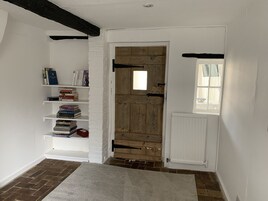 Um quarto com parede de tijolos brancos, porta de madeira, radiador branco e uma janela.