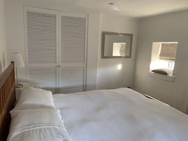 Quarto com cama, mesa de cabeceira, luminária, guarda-roupa, espelho e janela com vista.