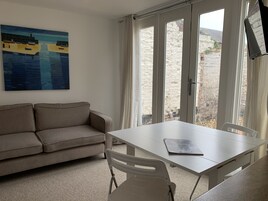 Quarto com sofá bege, mesa branca e uma grande janela com cortinas.