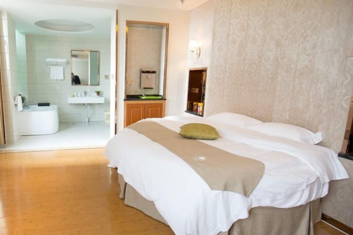 Quarto de hotel com uma cama grande, banheiro com banheira e um espelho.