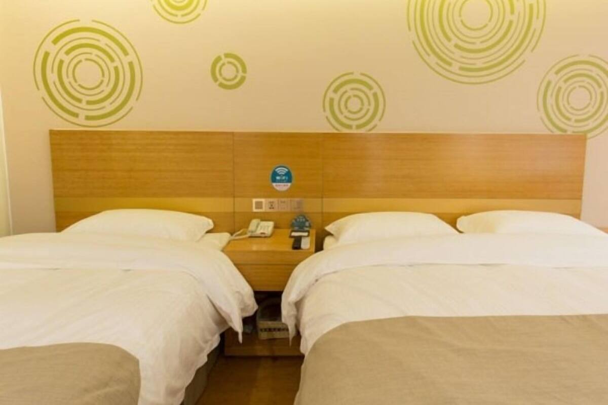 Quarto de hotel com duas camas, cabeceira de madeira, mesa de cabeceira com telefone e garrafa de água, e adesivos circulares na parede.