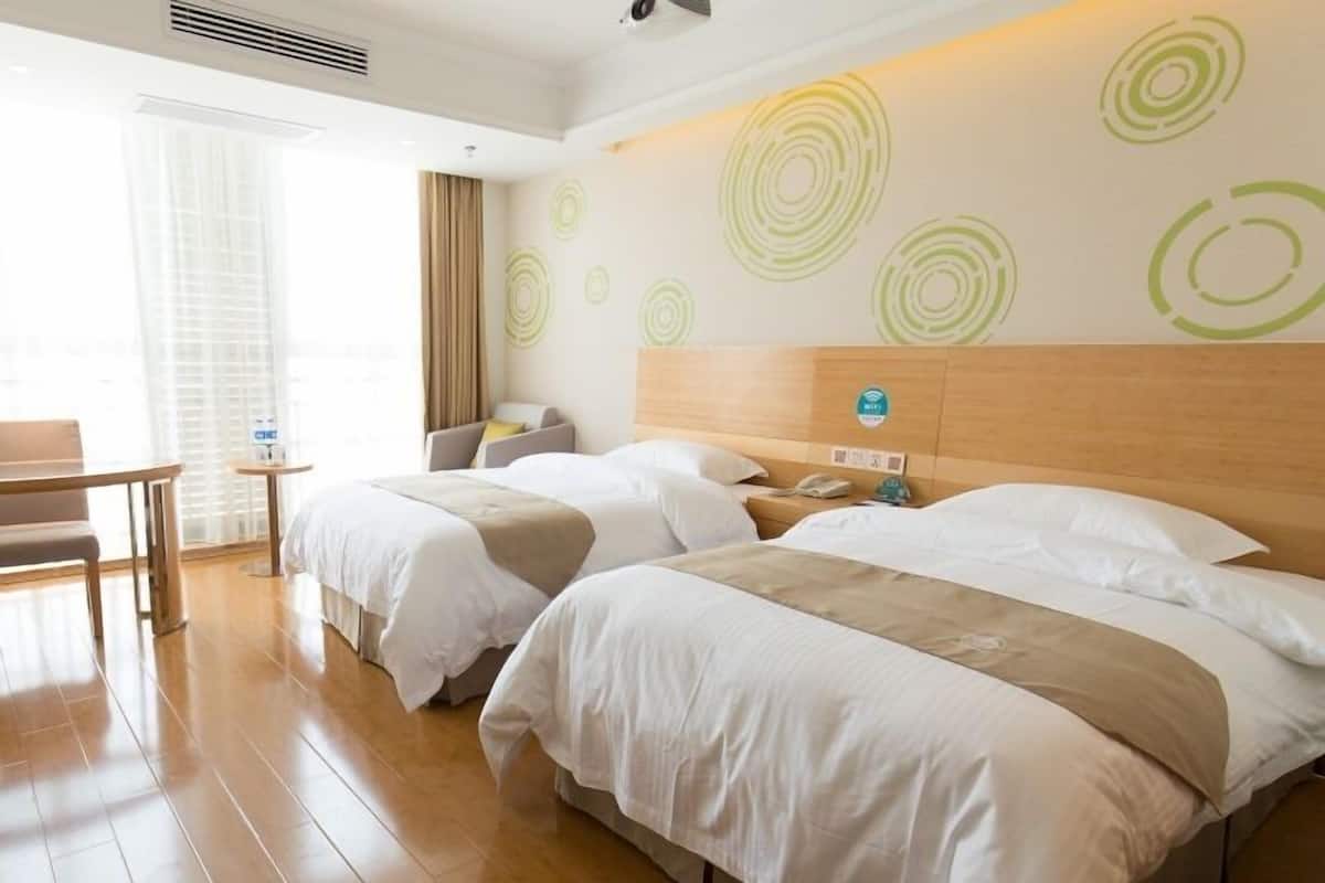 Quarto de hotel com duas camas, piso de madeira, uma escrivaninha e uma janela com cortinas.