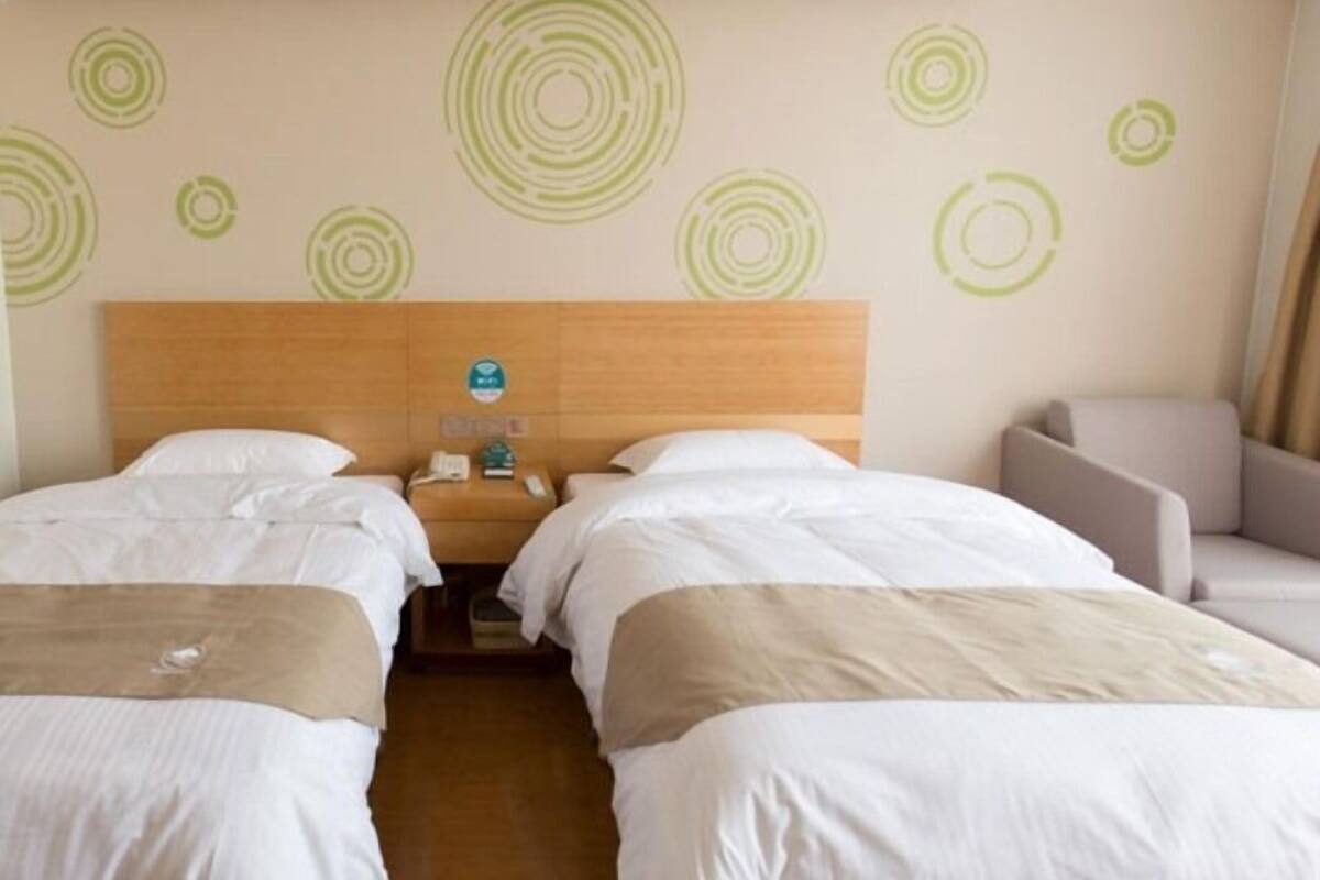 Quarto de hotel com duas camas, cabeceira de madeira, pequena mesa de cabeceira com um telefone e um livro, e parede com padrões circulares.