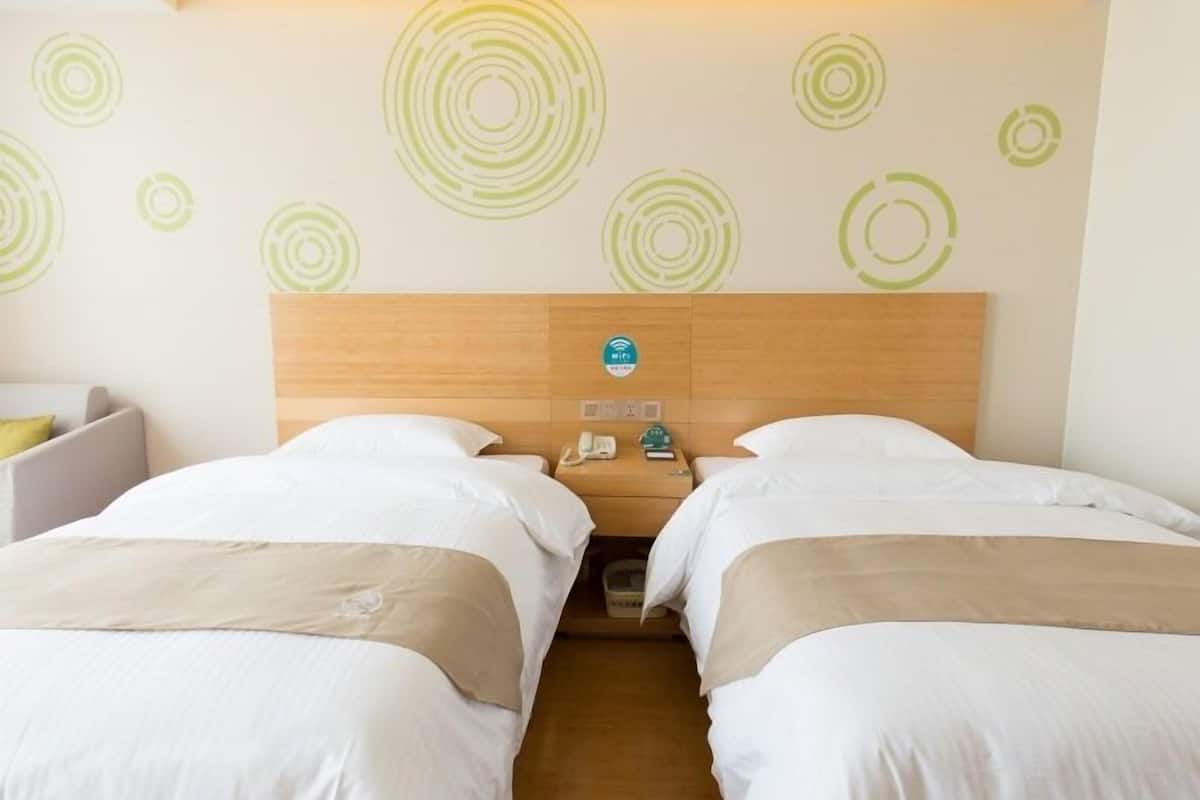 Quarto de hotel com duas camas, uma cabeceira de madeira, uma parede com desenhos circulares e uma mesinha de cabeceira com um telefone e um livro.