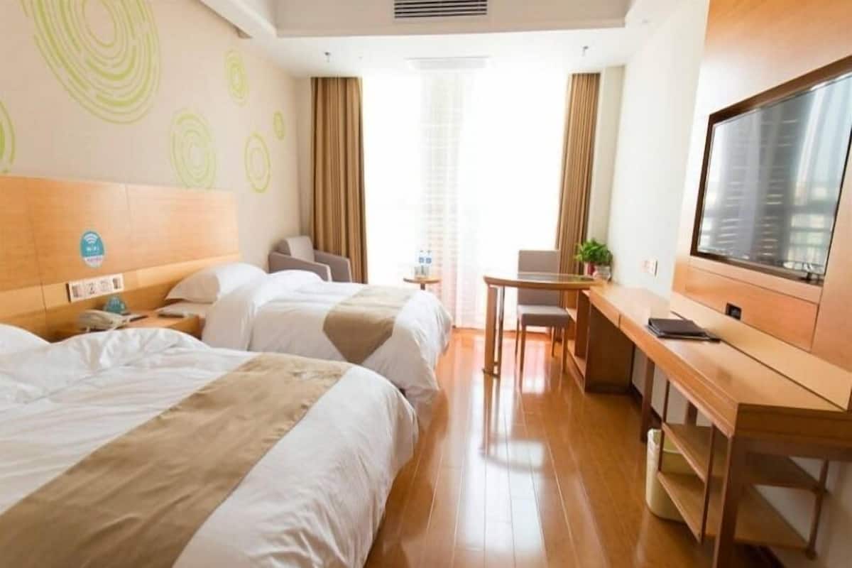 Quarto de hotel com duas camas, uma escrivaninha, uma cadeira, uma televisão e uma janela com cortinas.