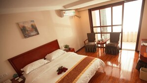 Quarto de hotel com uma cama grande, uma mesa de cabeceira com telefone, uma pequena mesa com cadeiras e uma janela com cortinas.
