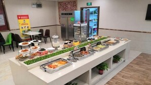 Uma área de buffet com diversos pontos de comida, uma geladeira e disposição de mesas e cadeiras.