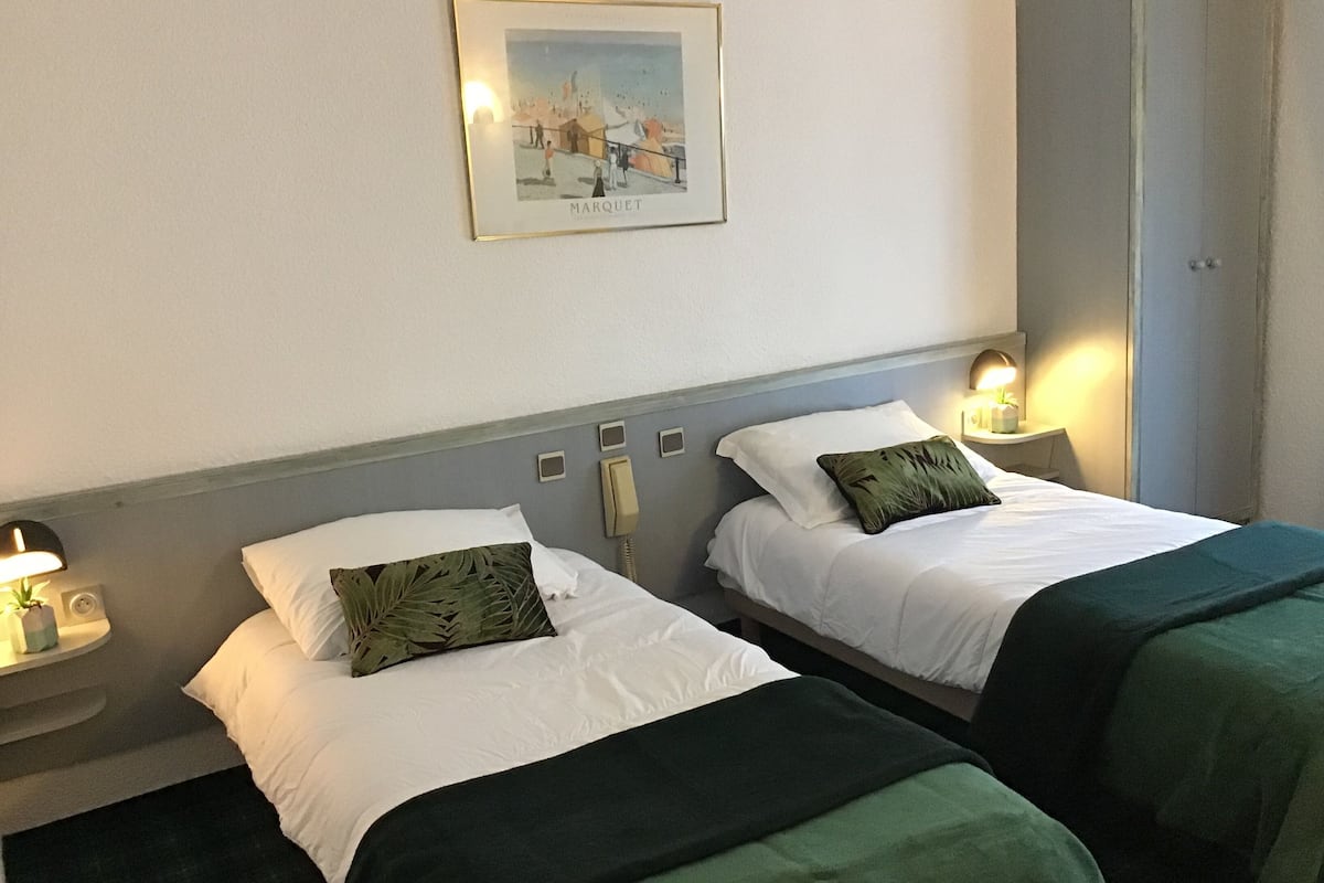Quarto de hotel com duas camas, mesa de cabeceira com abajur, telefone e quadro na parede.