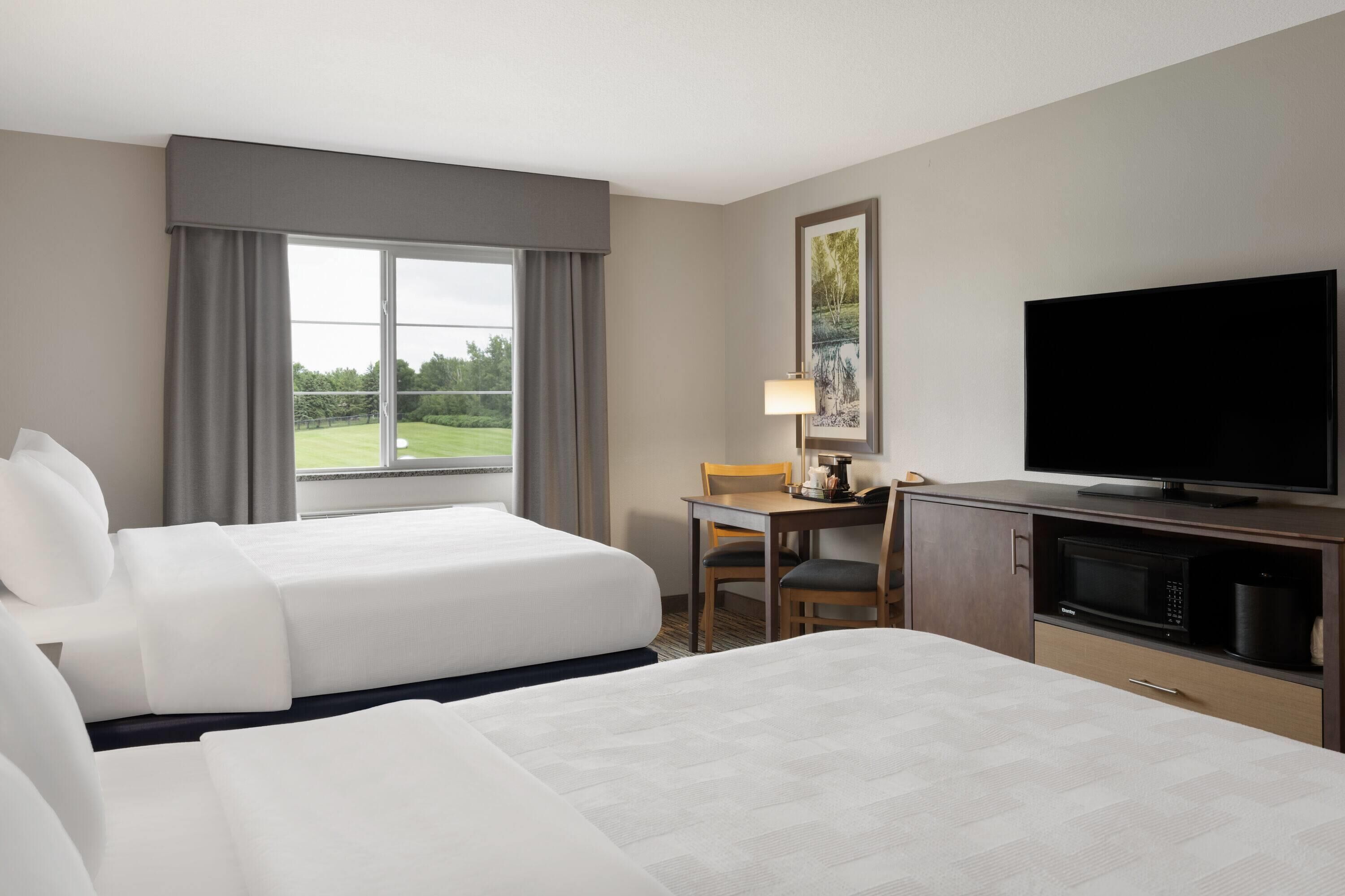 Quarto de hotel com duas camas, uma escrivaninha, televisão e micro-ondas.