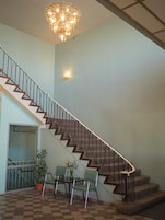 Uma escadaria com piso xadrez, um lustre e um espaço de estar com cadeiras e uma mesa.
