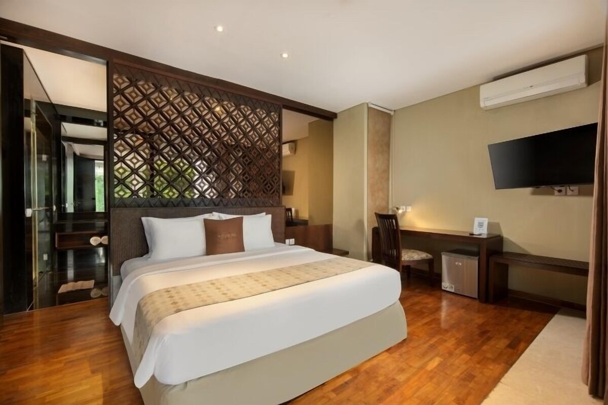 Quarto de hotel com uma cama grande, uma escrivaninha, uma cadeira, uma televisão e um painel decorativo na parede.