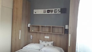 Quarto com cabeceira de madeira, telefone de apoio e prateleira com objetos decorativos.