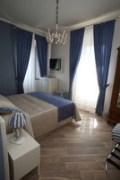 Um quarto com uma cama, mesa de cabeceira, luminária, cômoda, televisão e cortinas.