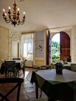 Uma sala de jantar com um candelabro, uma mesa posta para quatro pessoas e vista para o exterior através de uma porta aberta.