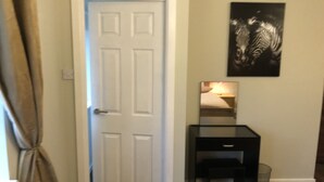 Um quarto com porta fechada, uma escrivaninha com candeeiro e uma obra de arte com tema de zebra na parede.