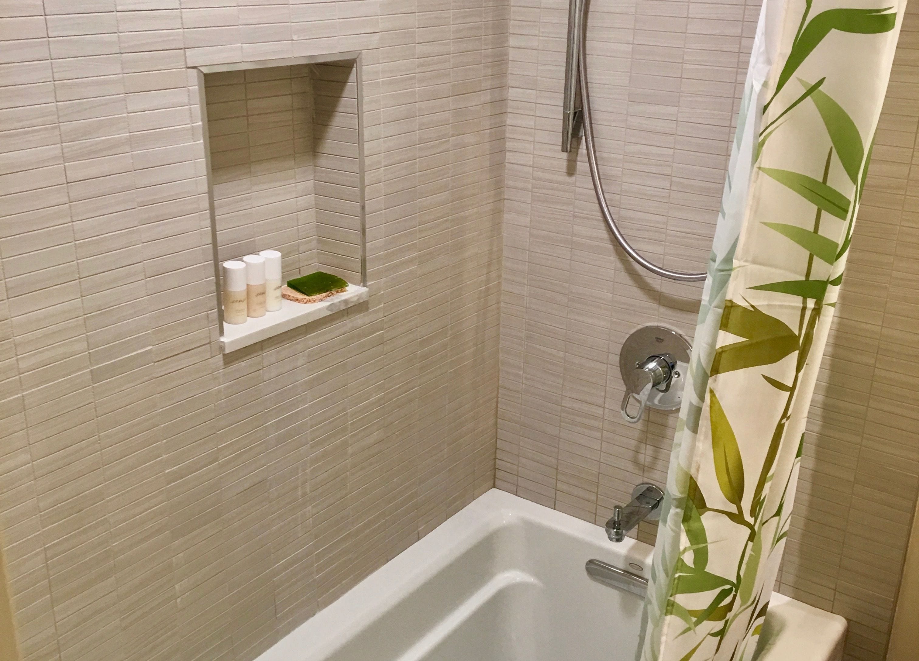 Uma casa de banho com uma banheira branca, um chuveiro com cortina de chuveiro estampada com motivos de bambu e uma prateleira com artigos de higiene pessoal.